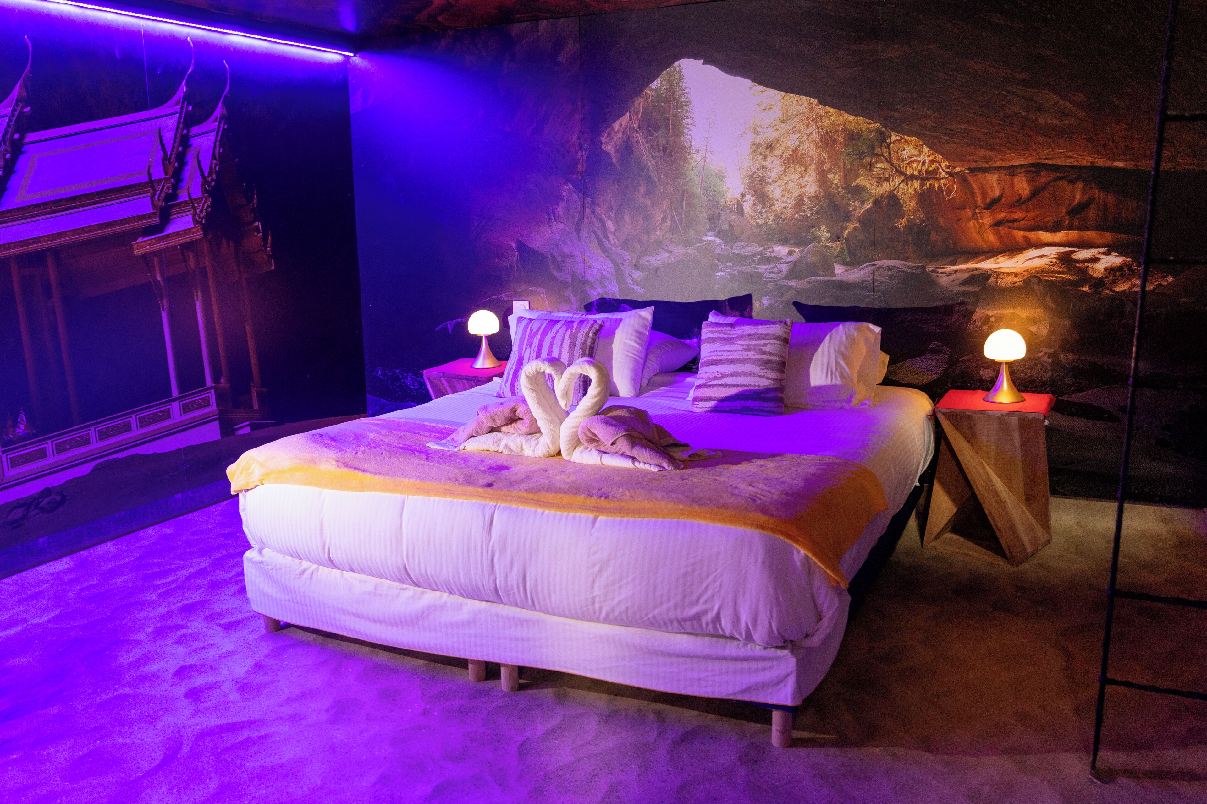 Quarto com cama, almofadas, cobertor e duas luminárias de cabeceira.