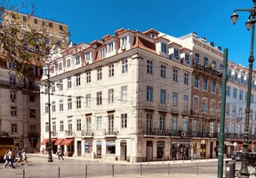 Um edifício de vários andares com estilo arquitetônico clássico, apresentando uma entrada de canto, várias janelas e sacadas.