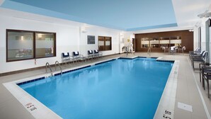 Uma grande piscina interior com faixas delimitadoras claras, cadeiras de descanso próximas e posto de salva-vidas.