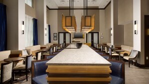 Um hall de hotel com um balcão de recepção extenso, diversas áreas de estar e um lustre grande.