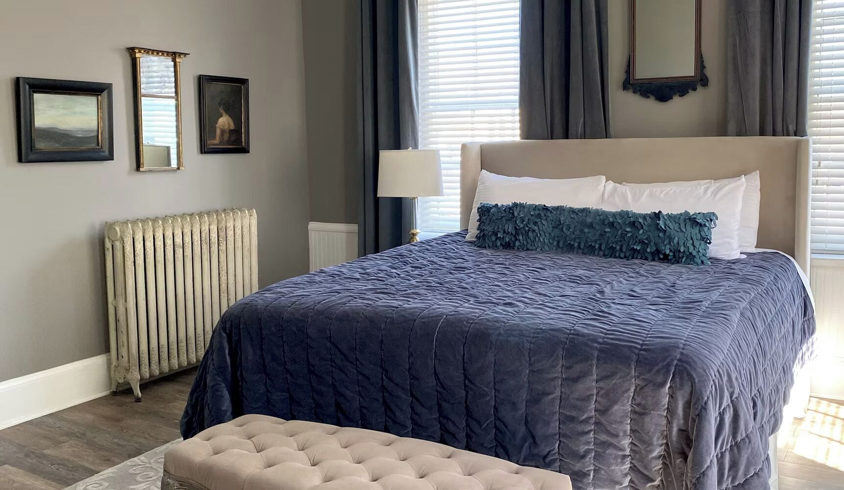 Quarto com cama, radiador, luminária e janela com cortinas.