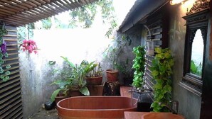 Uma área externa rústica com um grande barril de madeira, vasos de terracota e plantas em vasos.