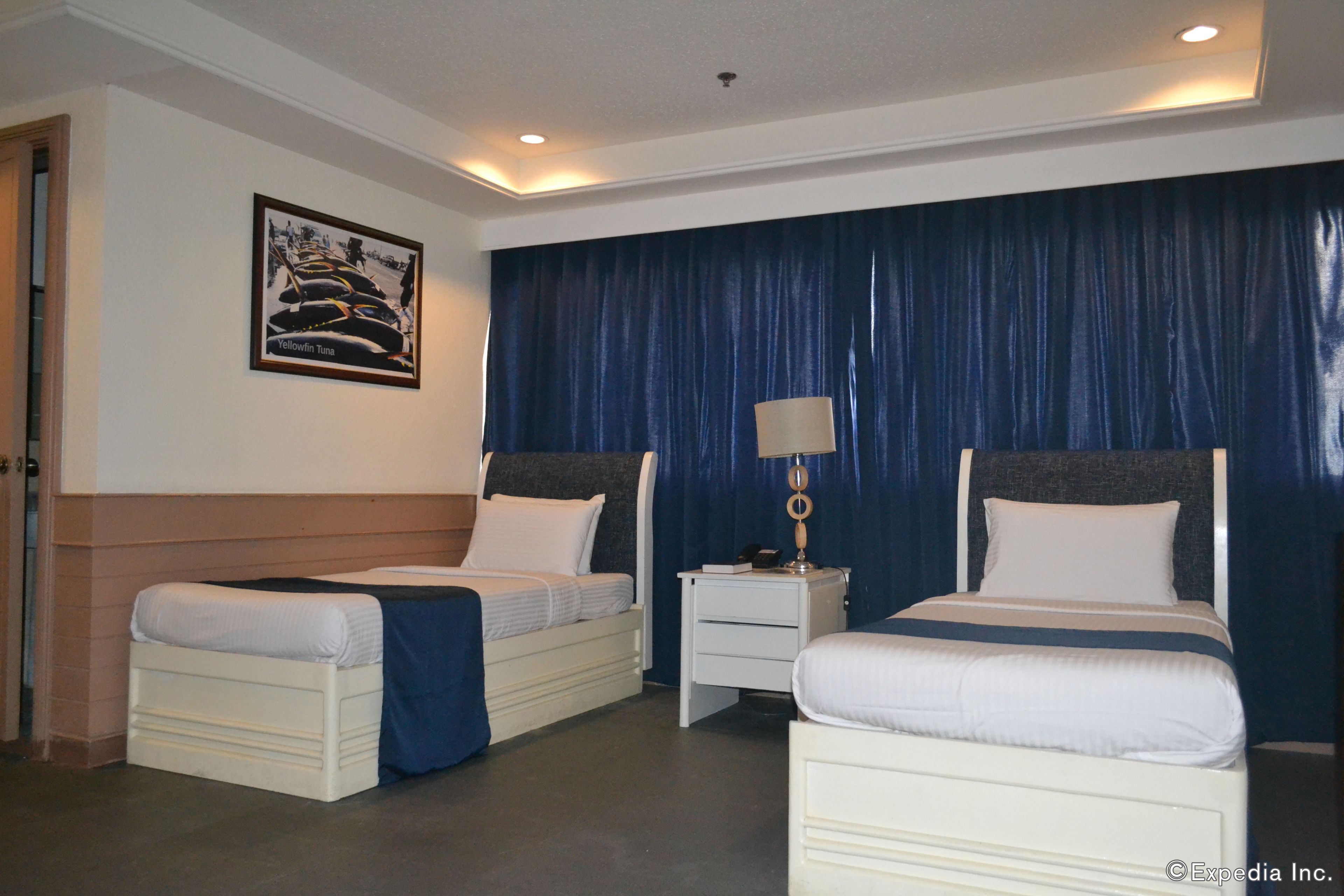 Quarto de hotel com duas camas de solteiro, mesa de cabeceira com abajur e um quadro na parede.