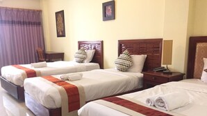 Quarto de hotel com três camas, cada uma com cabeceira de madeira, roupa de cama branca e detalhes em laranja. Há duas mesas de cabeceira com abajures, uma cadeira e um quadro na parede.
