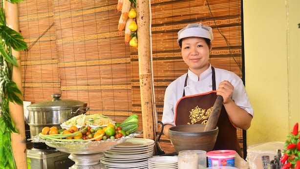 Um chef com uma wok grande, rodeado por diversos alimentos e utensílios de cozinha.