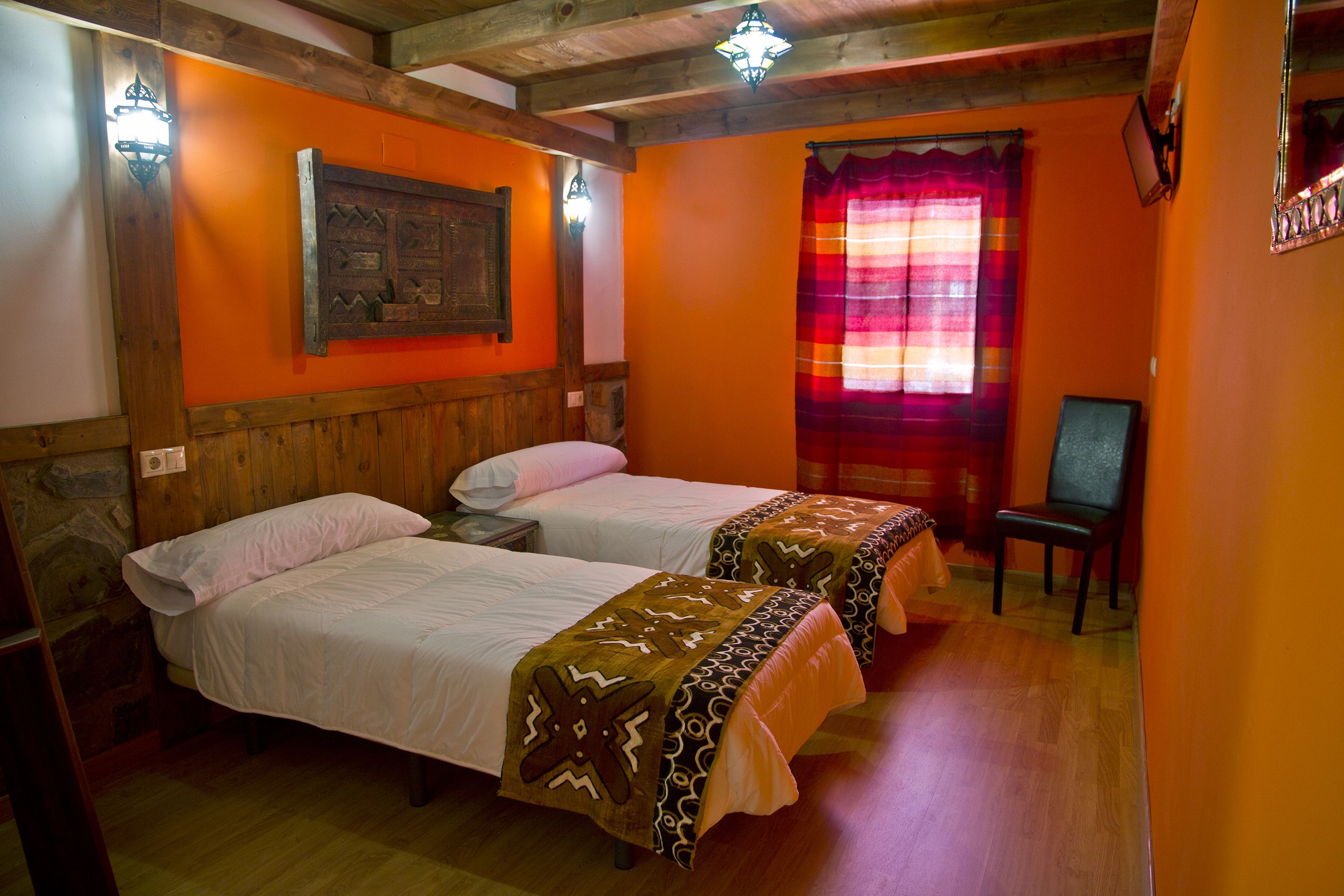 Quarto com duas camas, paredes de madeira, parede de destaque em pedra e cortina vermelha.