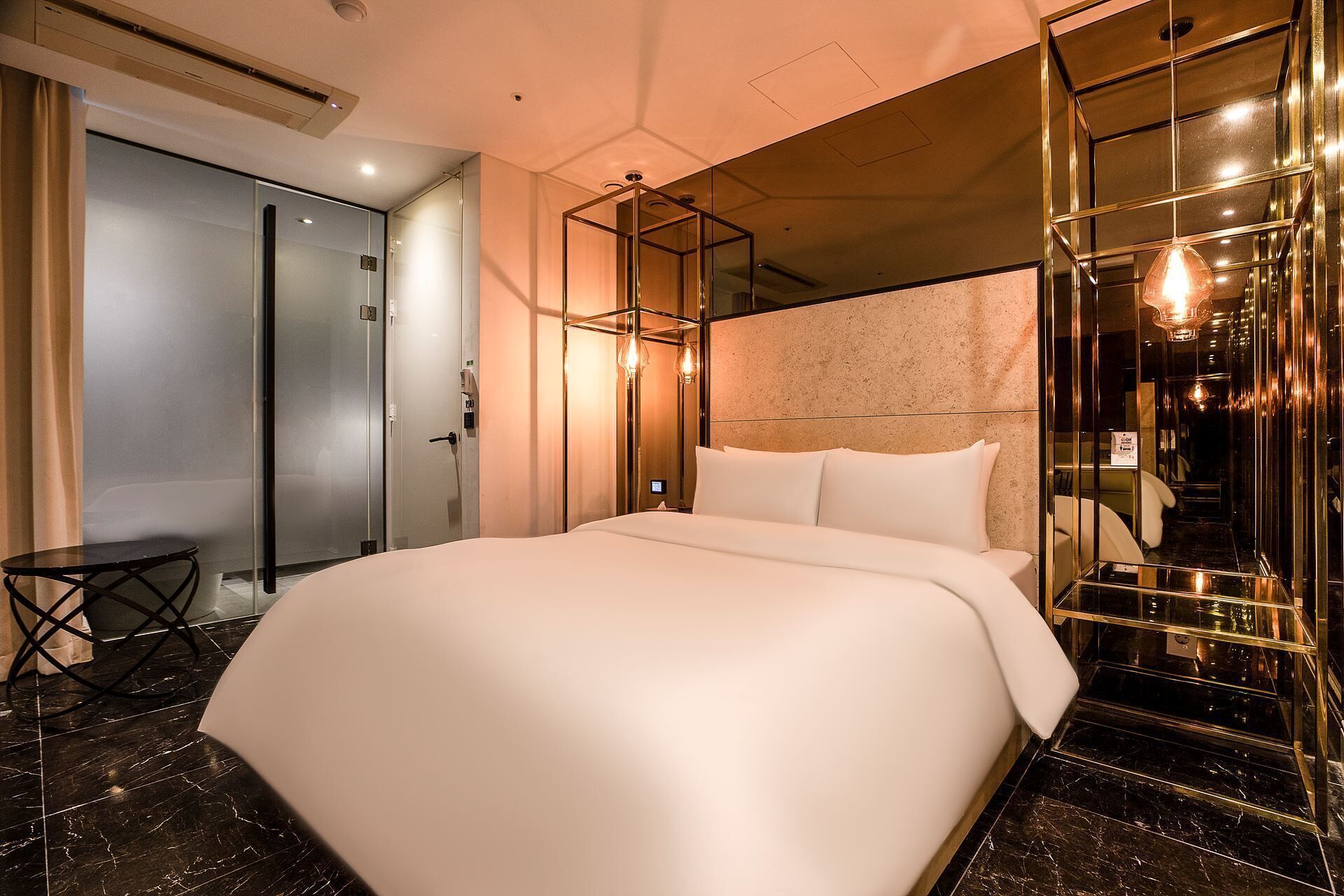 Quarto de hotel moderno com uma cama grande, divisória de vidro e piso de mármore.