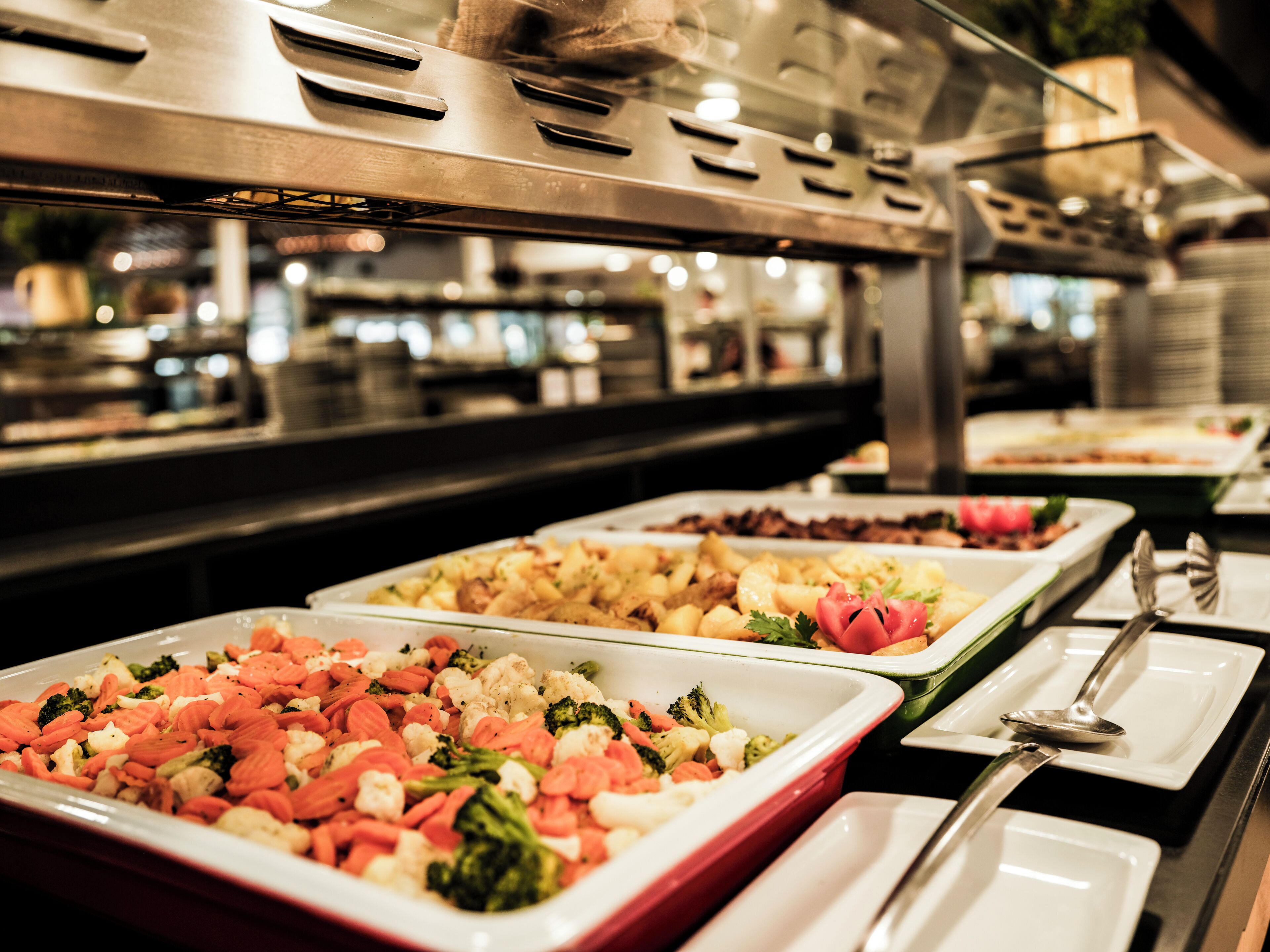 Buffet com diversos pratos, incluindo legumes e carnes, dispostos em bandejas.