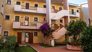 Um edifício residencial com vários andares, varandas, uma escadaria central e uma pequena área de jardim com flores.