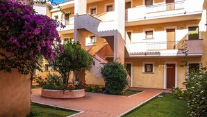 Um pátio com caminho de tijolos, um jardim central com flores e um edifício com várias varandas e janelas.