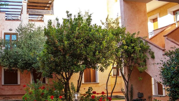 Um pátio central com um jardim de flores vermelhas, rodeado por edifícios com varandas e janelas.