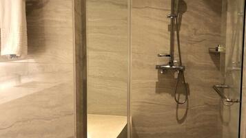 Uma casa de banho moderna com chuveiro em cabine de vidro, um porta-toalhas e um banco.