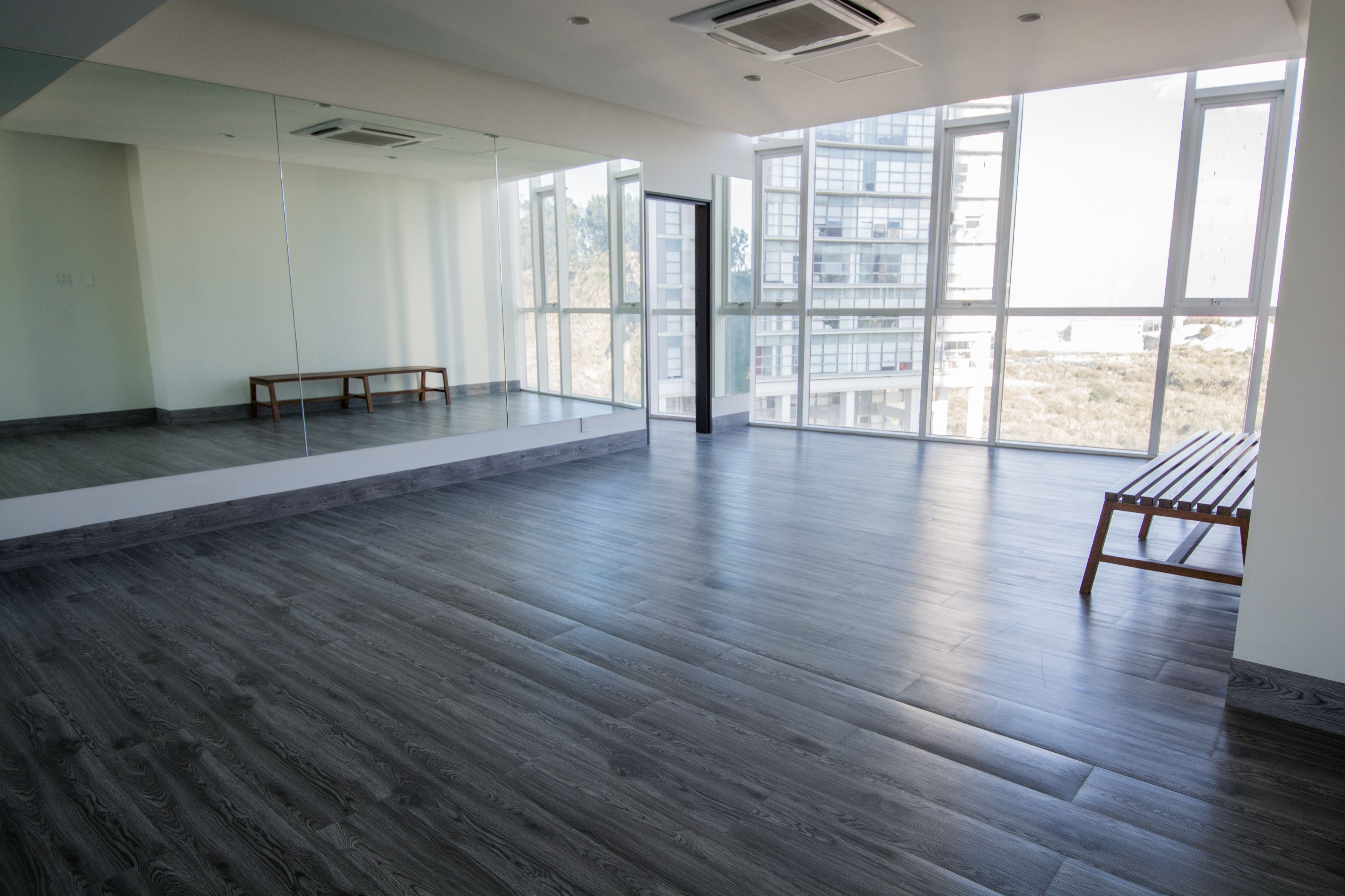 Quarto espaçoso com um espelho grande, bancos de madeira e janelas amplas com vista para edifícios e paisagem.