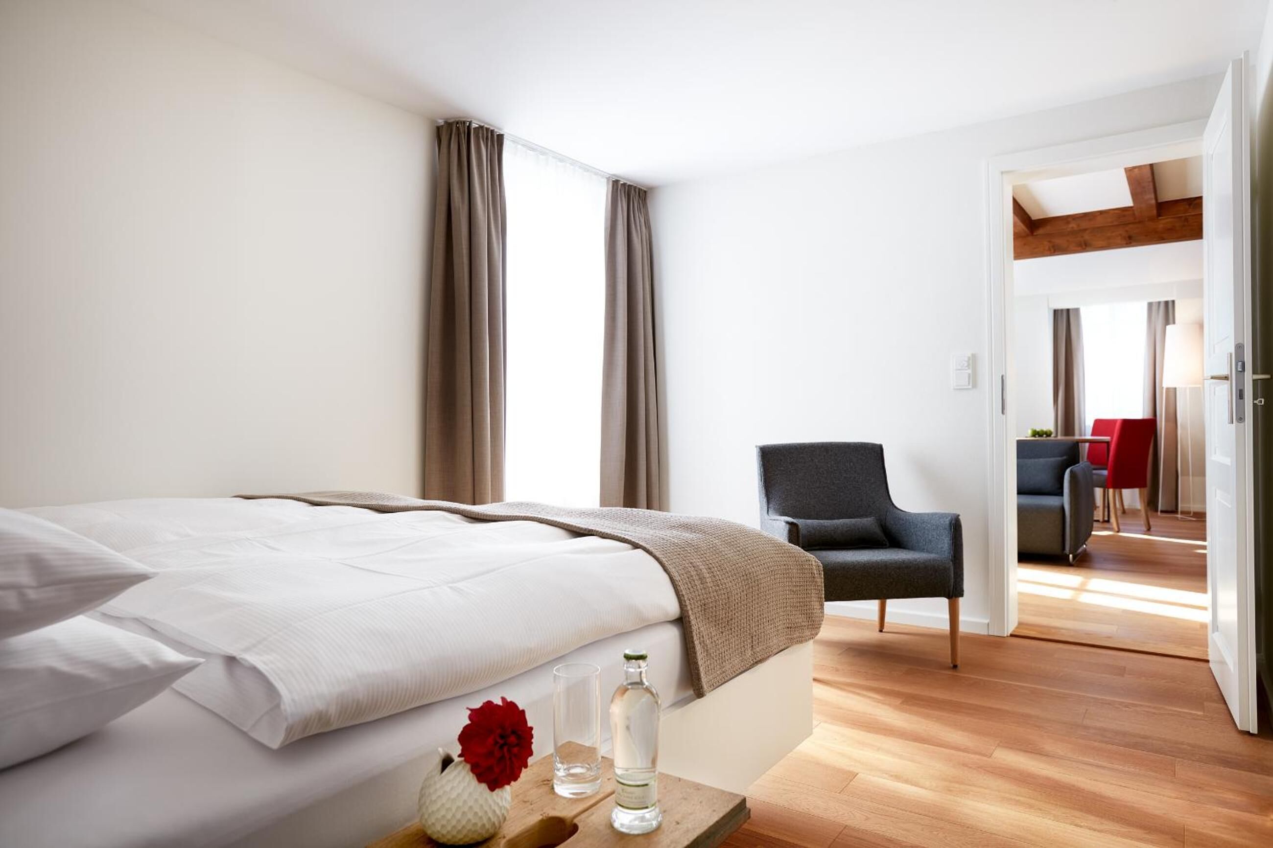 Quarto de hotel moderno com uma cama grande, uma cadeira e vista para a área de refeições.