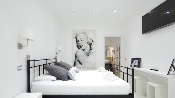 Quarto moderno com cama, um quadro, TV e banheiro visível ao fundo.