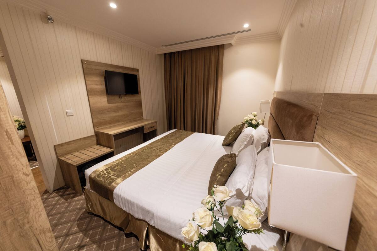 Quarto de hotel com cama, escrivaninha, TV fixada na parede e janela com cortinas.