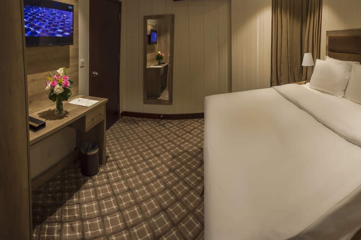 Quarto de hotel com uma cama grande, uma mesa com um vaso de flores, uma televisão na parede e um espelho.