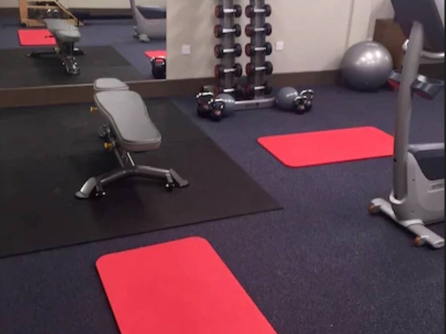 Uma academia com equipamentos de exercício, tapetes vermelhos e um espelho.