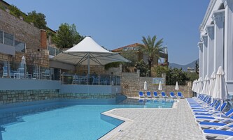 Uma área de piscina com cadeiras de descanso azuis e guarda-sóis, paredes de pedra e céu claro.