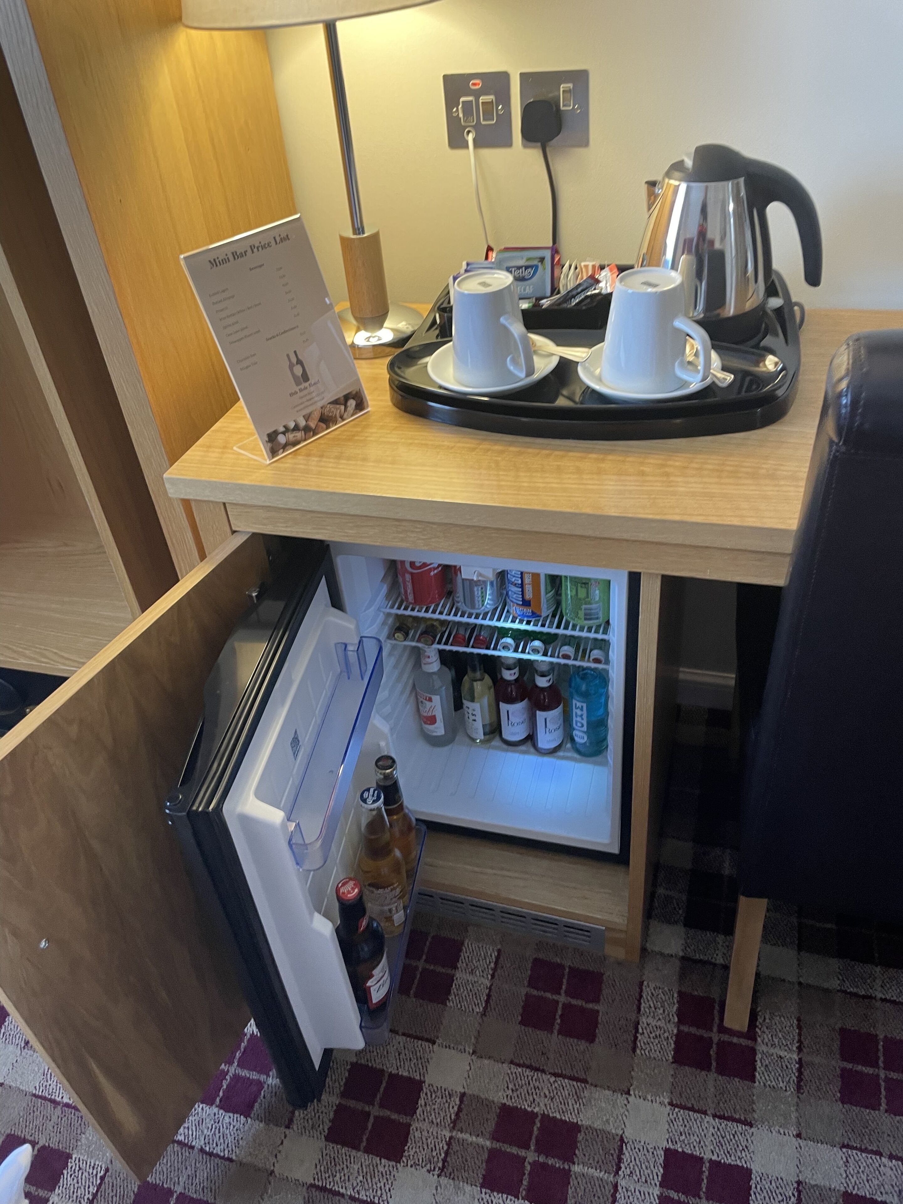 Uma kitchenette compacta com geladeira, um minibar com lista de preços, chaleira e uma bandeja com xícaras e cafeteira.