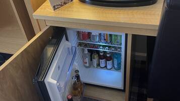 Uma kitchenette compacta com geladeira, um minibar com lista de preços, chaleira e uma bandeja com xícaras e cafeteira.