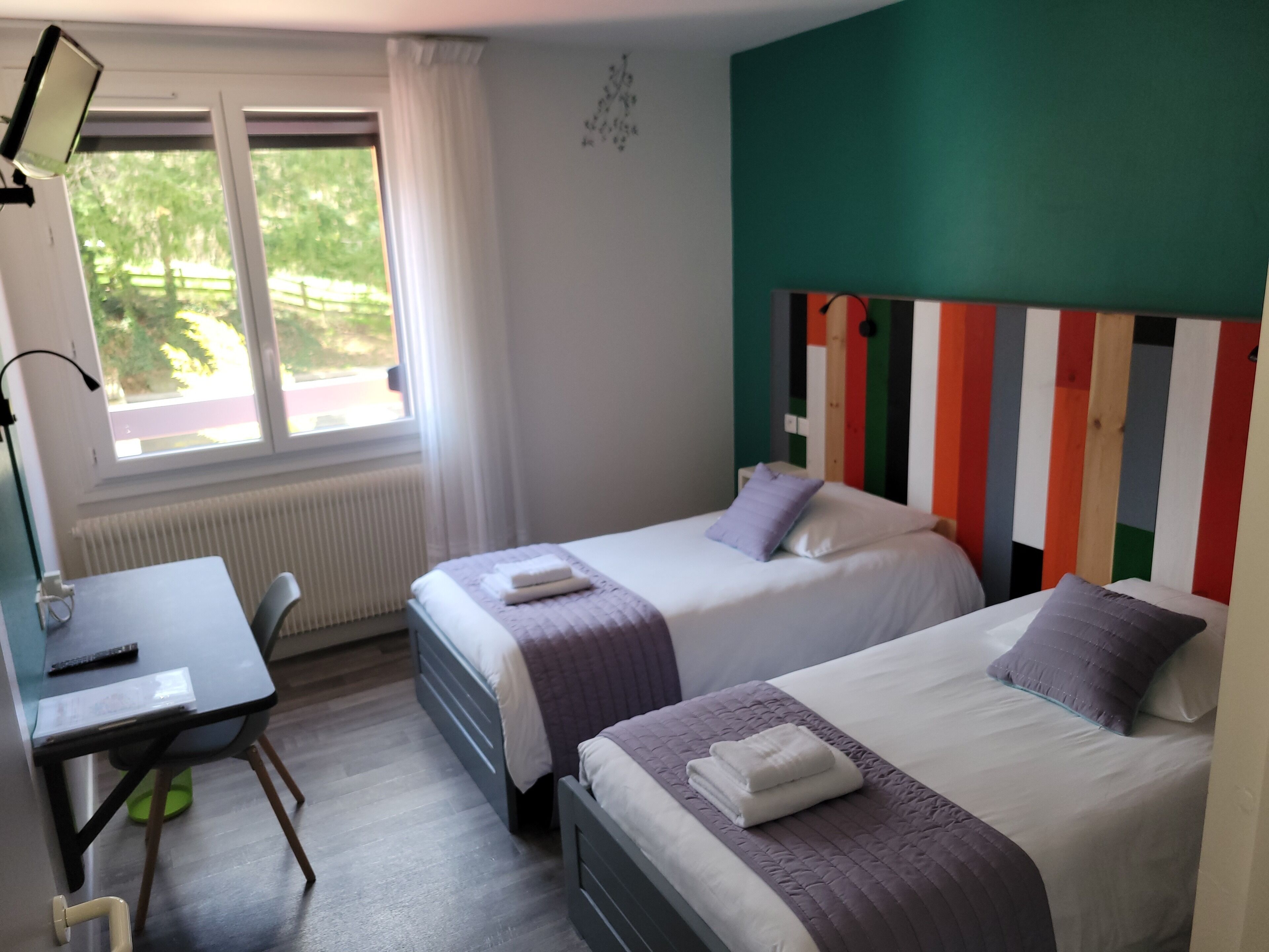 Quarto de hotel com duas camas, uma escrivaninha e uma janela com cortinas.