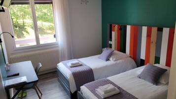 Quarto de hotel com duas camas, uma escrivaninha e uma janela com cortinas.