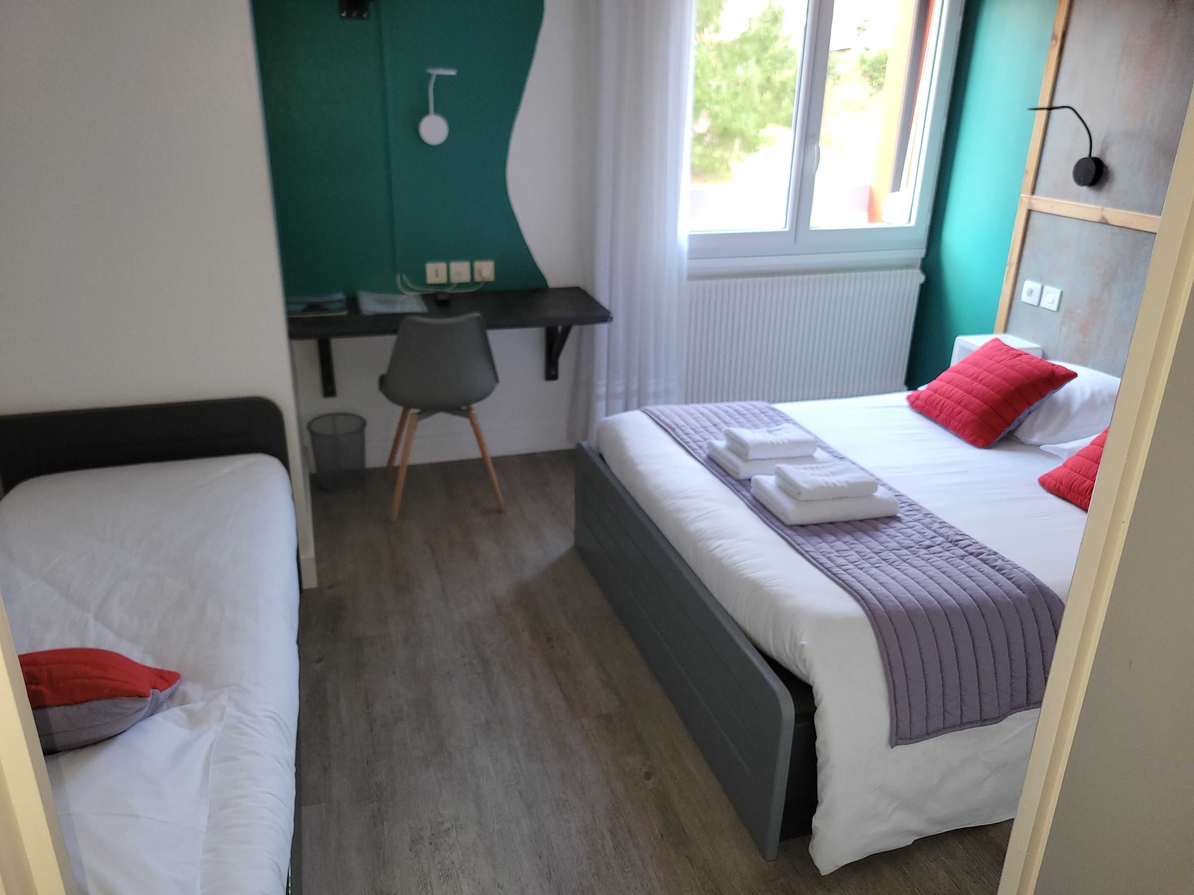 Quarto de hotel com duas camas, uma escrivaninha e uma cadeira.