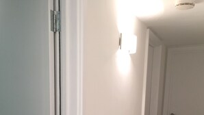 Um corredor estreito com paredes brancas, um interruptor de luz e uma porta no final.