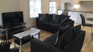 Uma sala de estar moderna com um sofá preto, uma TV de tela plana e uma mesa de centro com um rendado.