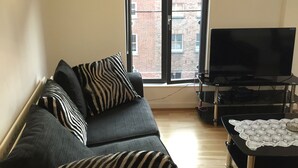 Uma sala de estar com sofá, televisão e janela com vista para um edifício de tijolos.