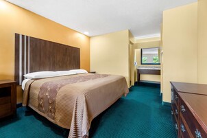 Quarto de hotel com uma cama, cômoda, escrivaninha com espelho e vista para o exterior.