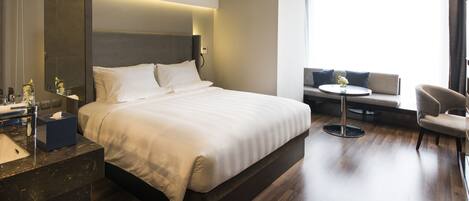 Quarto de hotel moderno com uma cama grande, uma mesa redonda, um sofá e um banheiro com bancada de mármore.