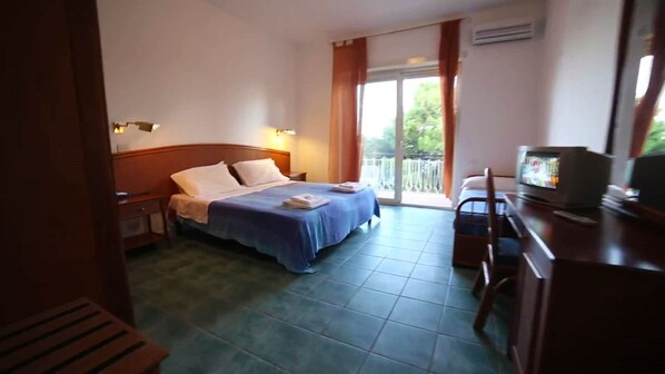 Quarto de hotel com cama, escrivaninha com televisão e varanda com vista.