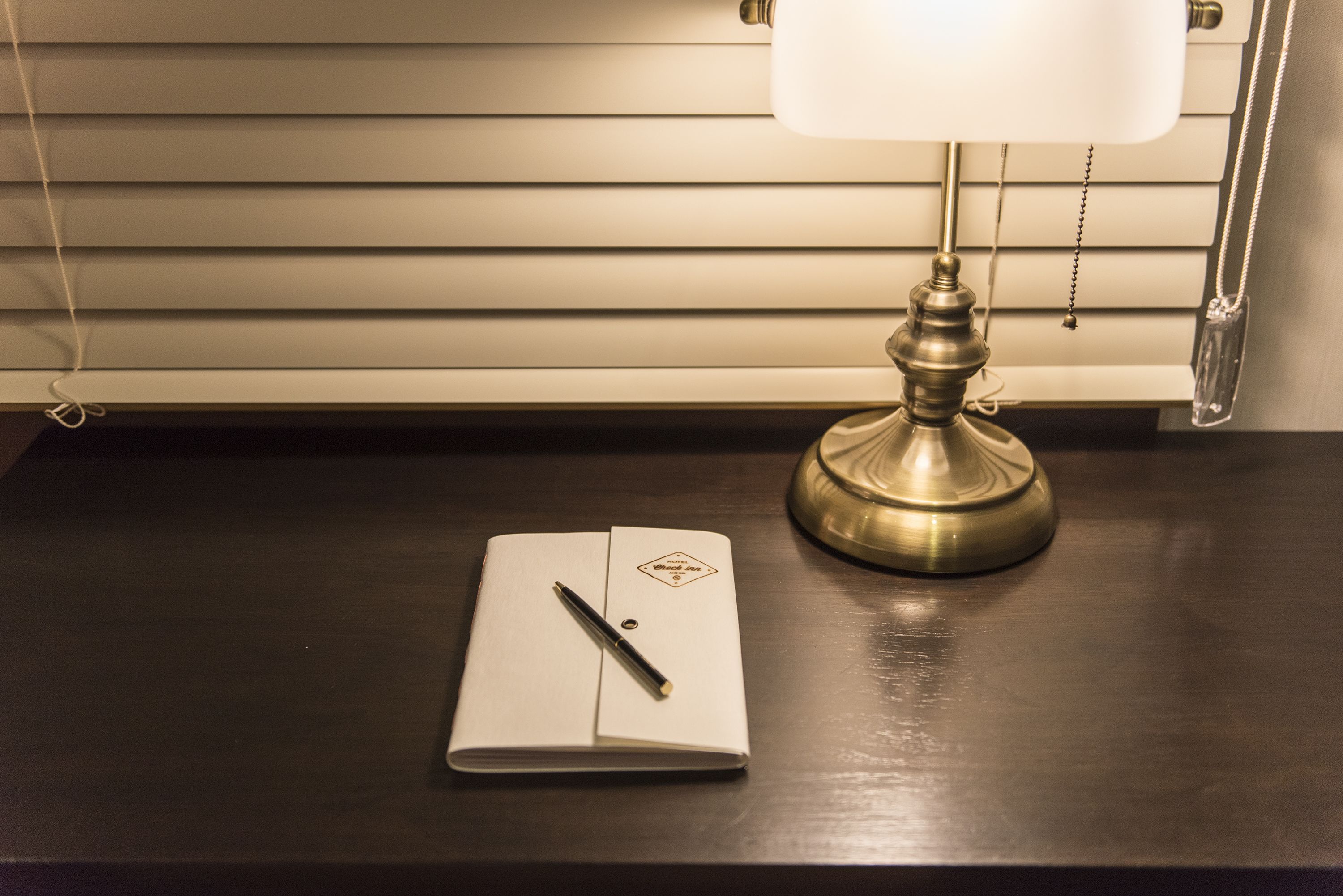 Uma mesa com uma luminária, um caderno e uma caneta.