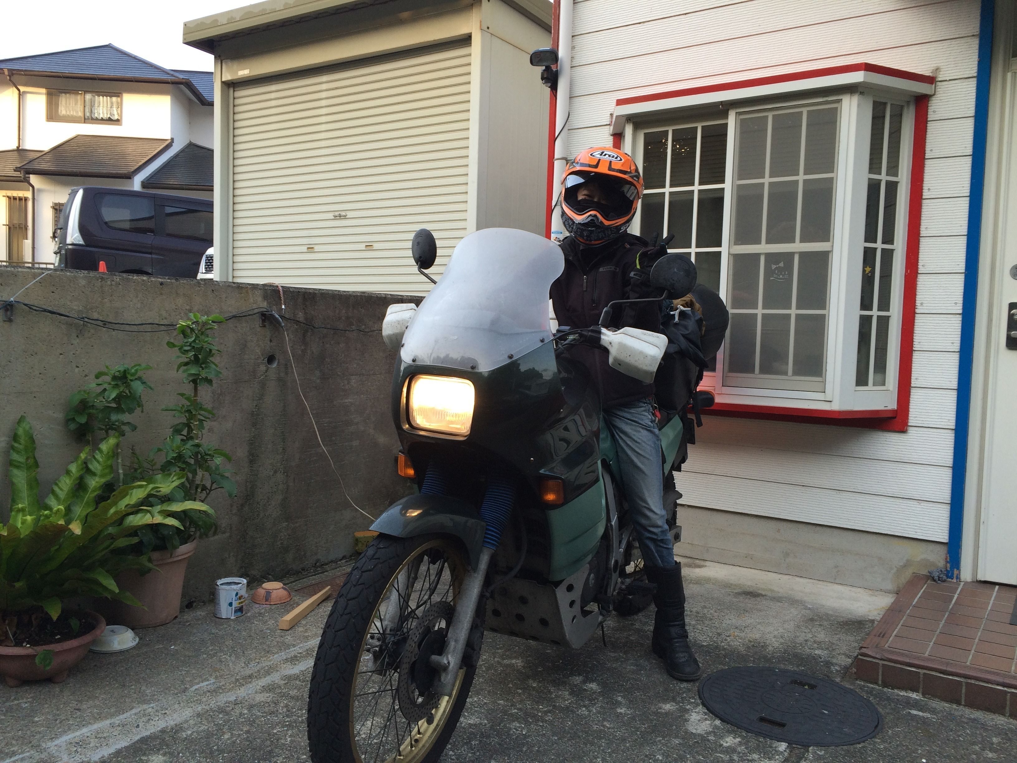 Uma motocicleta estacionada em frente a uma casa com porta de garagem e janela com moldura vermelha.