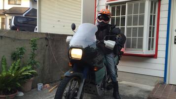 Uma motocicleta estacionada em frente a uma casa com porta de garagem e janela com moldura vermelha.