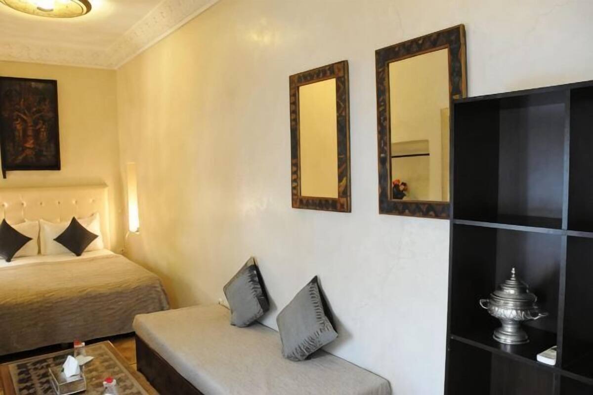 Quarto de hotel com cama, sofá, duas espelhas e um prato de prata decorativo.