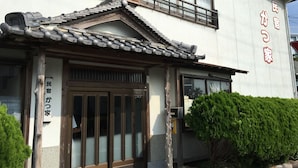 Um edifício tradicional japonês com telhado de telhas, portas de madeira e uma placa indicando que é uma pensão.