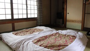 Um quarto japonês tradicional com tatames, futon com manta estampada, porta deslizante e televisão ao fundo.
