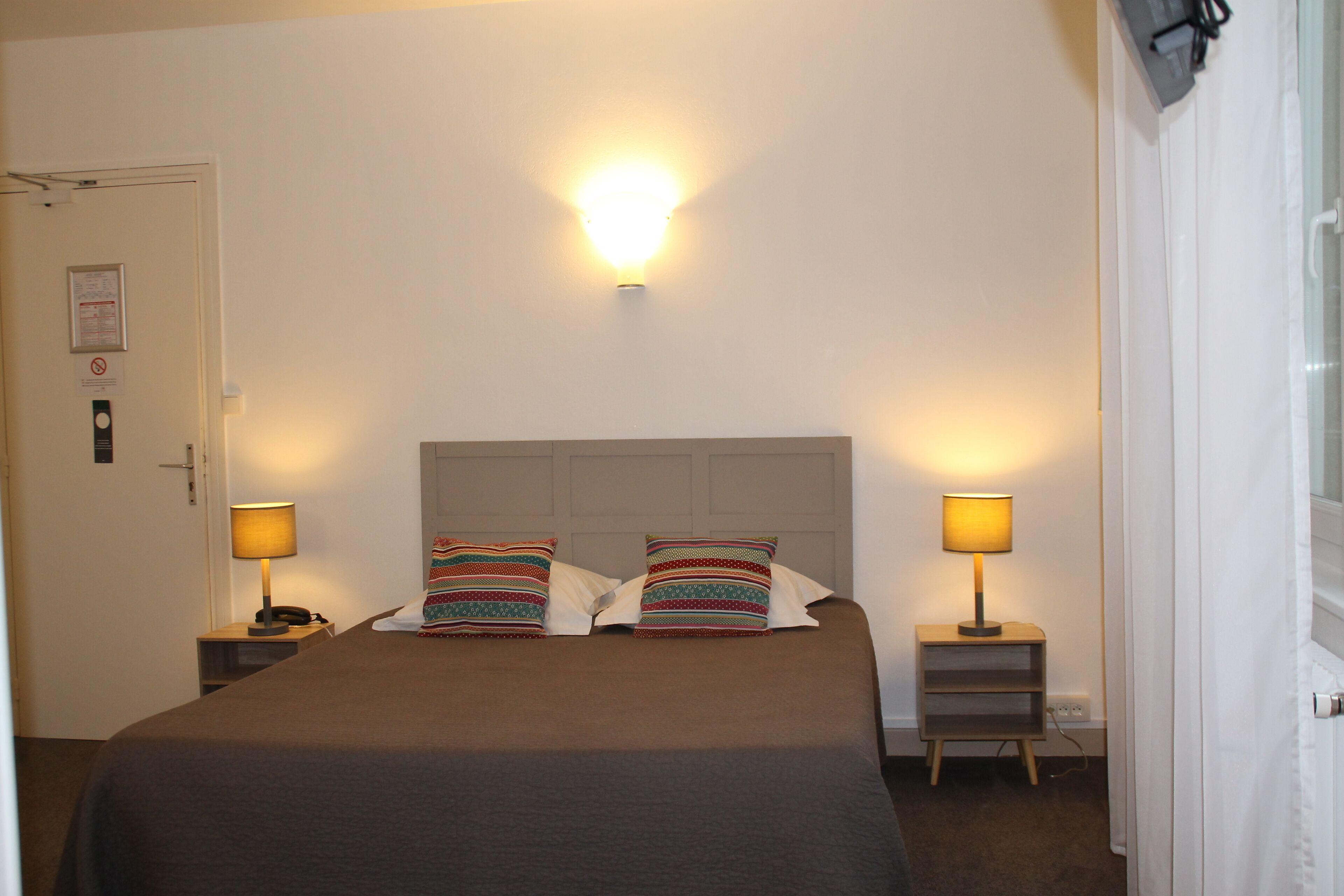 Quarto de hotel com cama, duas luminárias de cabeceira, mesa de cabeceira e luminária na parede.