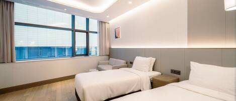 Quarto de hotel moderno com duas camas, área de estar e grandes janelas com vista para a cidade.