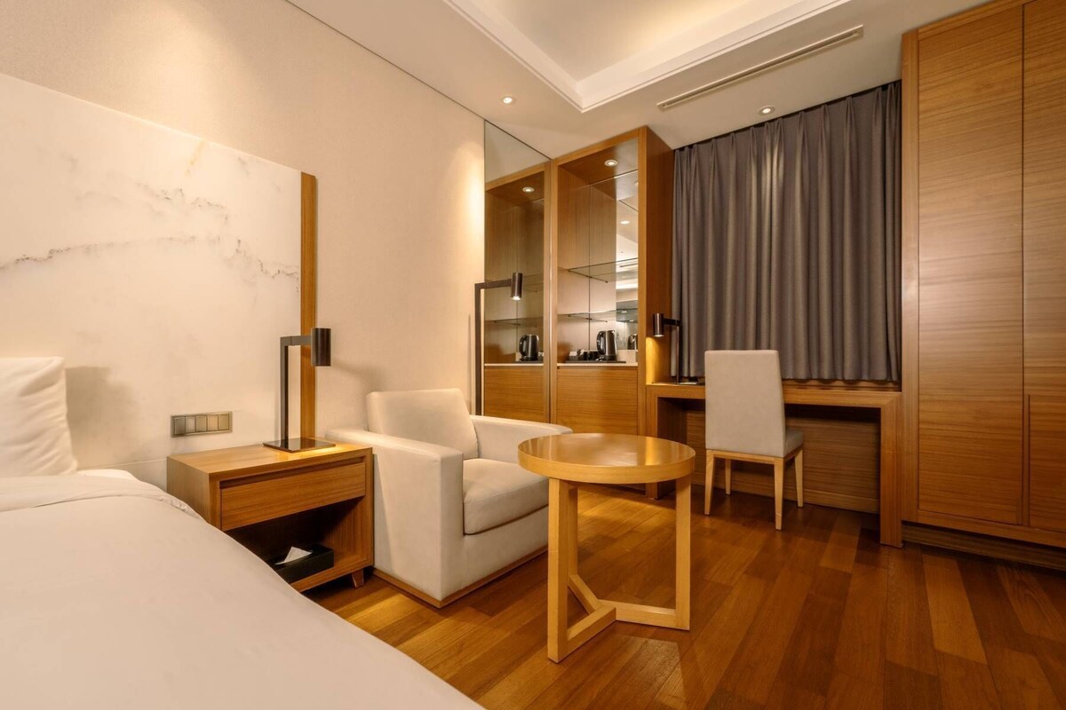Quarto de hotel moderno com uma cama, escrivaninha, cadeira e uma pequena mesa.