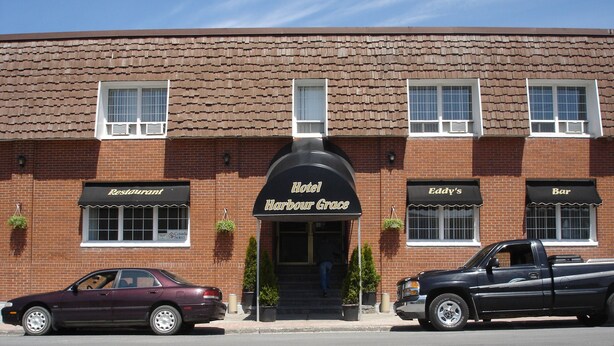Um edifício de tijolos com a placa Hotel Harbour Grace, um restaurante e um bar.