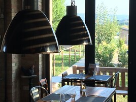 Uma área de refeições com mesa posta para dois, vista para o verde e montanhas, e duas luminárias pendentes.