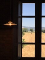 Quarto com uma grande janela, luminária pendente e vista para uma paisagem rural.
