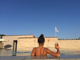 Uma pessoa em uma piscina, com céu azul límpido e uma bandeira ao fundo.
