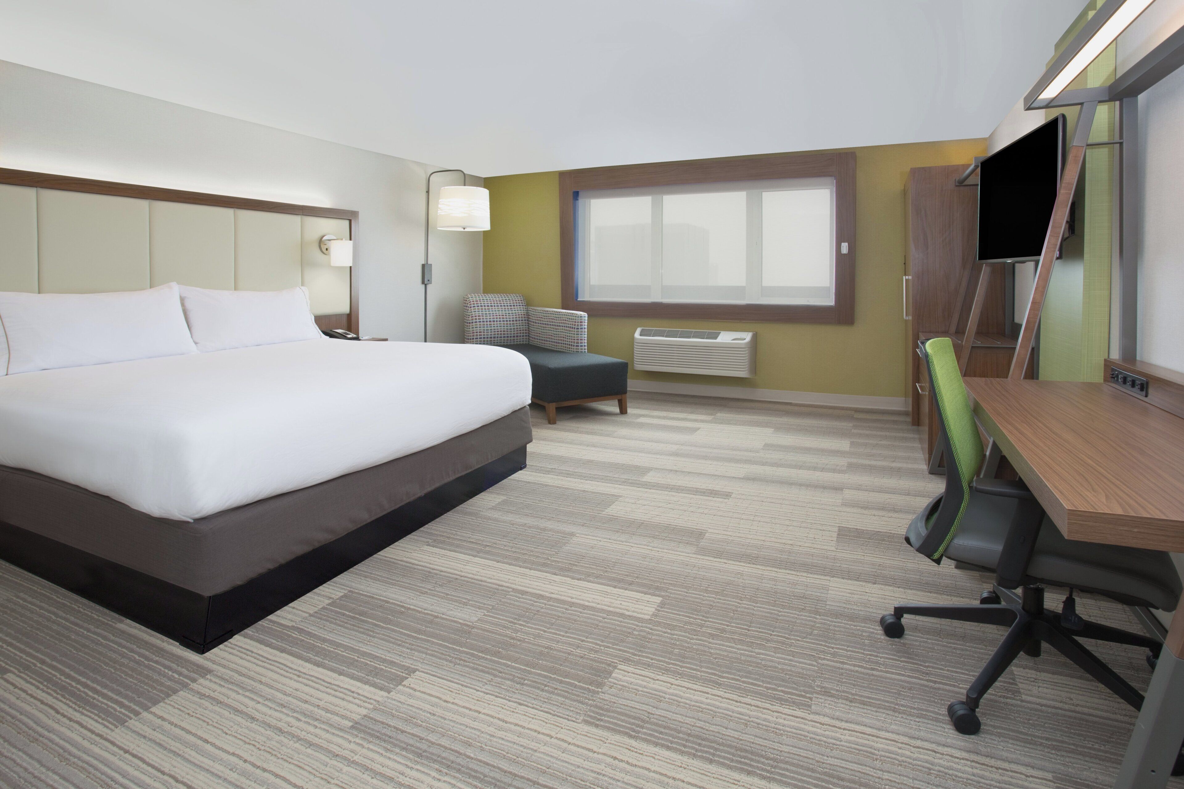 Quarto de hotel com uma cama grande, uma escrivaninha, uma cadeira, uma televisão e uma janela.