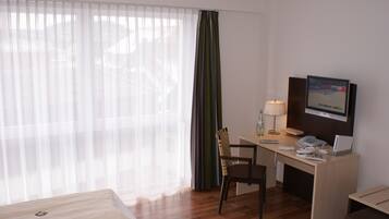 Quarto de hotel com cama, secretária com computador, cadeira, luminária e televisão.