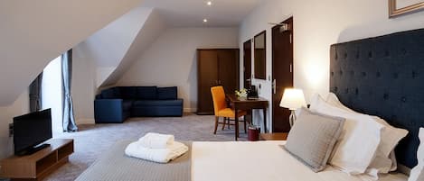 Quarto de hotel com uma cama grande, televisão, sofá e secretária com cadeira.